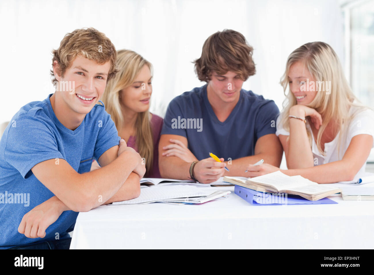 A group of students sitting together as they all study as one sits ...