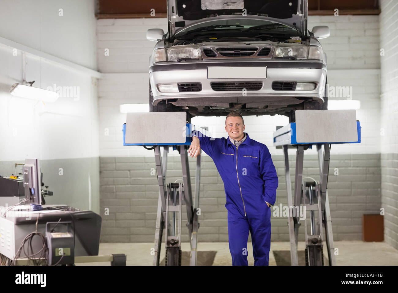 Smiling mechanic leaning on a machine below a car Stock Photo - Alamy