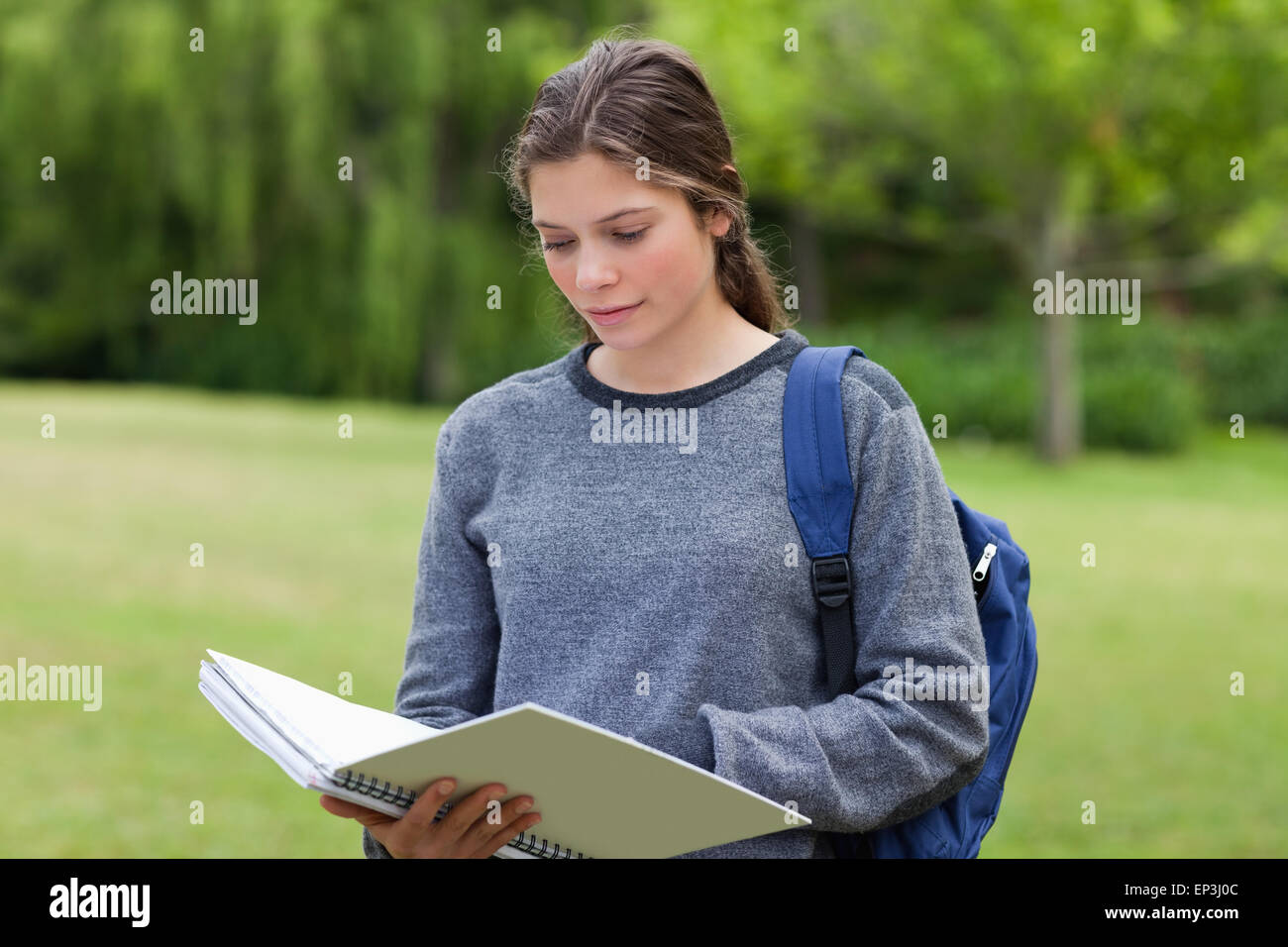 Young serious woman reading her notebook while standing in a park Stock ...