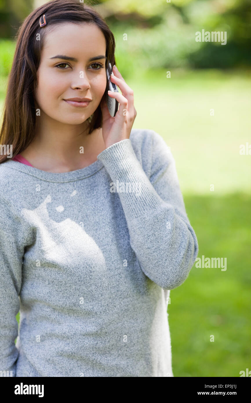 Young serious woman calling with her cellphone while standing in a park ...