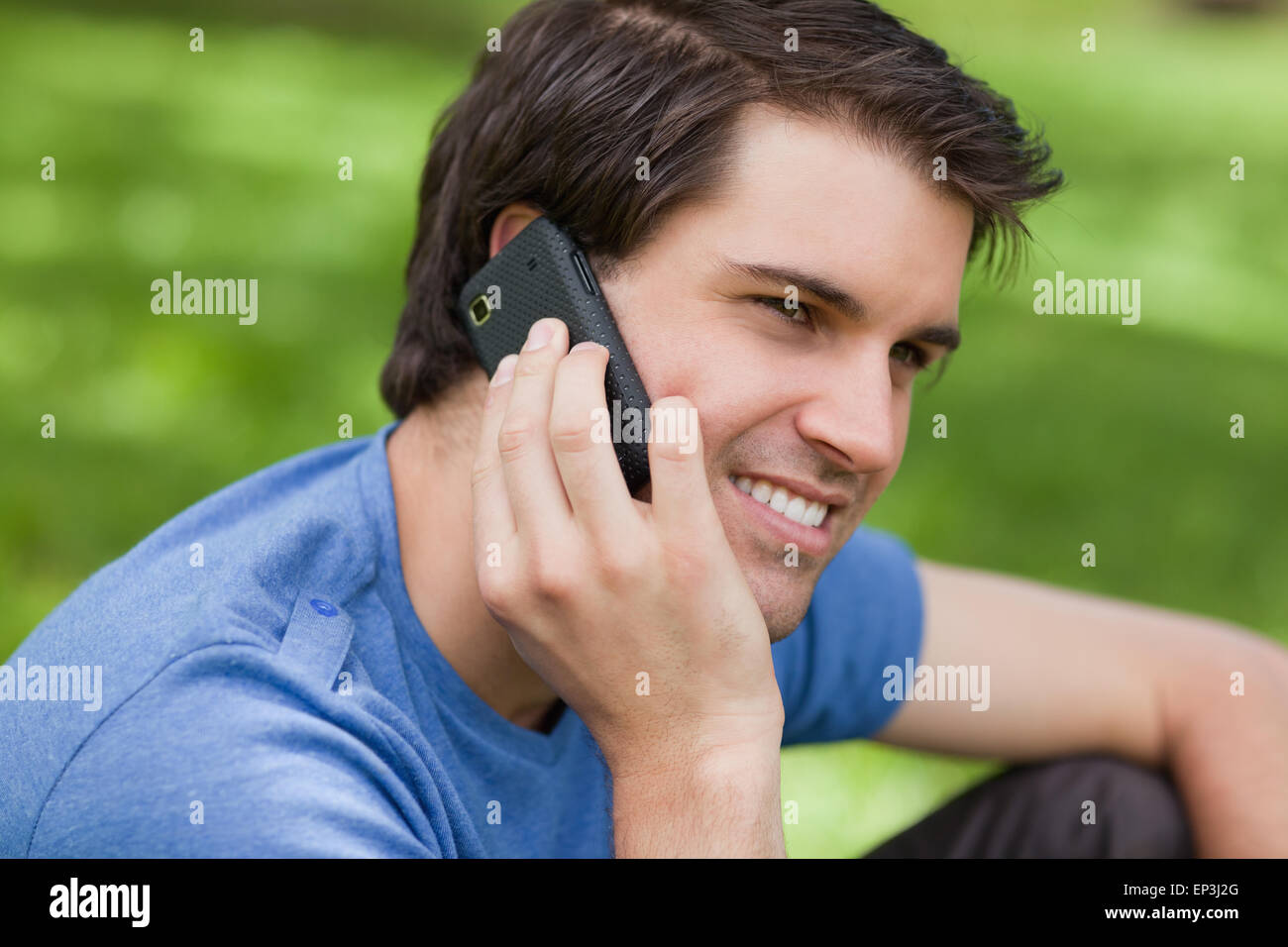 Smiling young man sitting in the countryside while using his cellphone ...