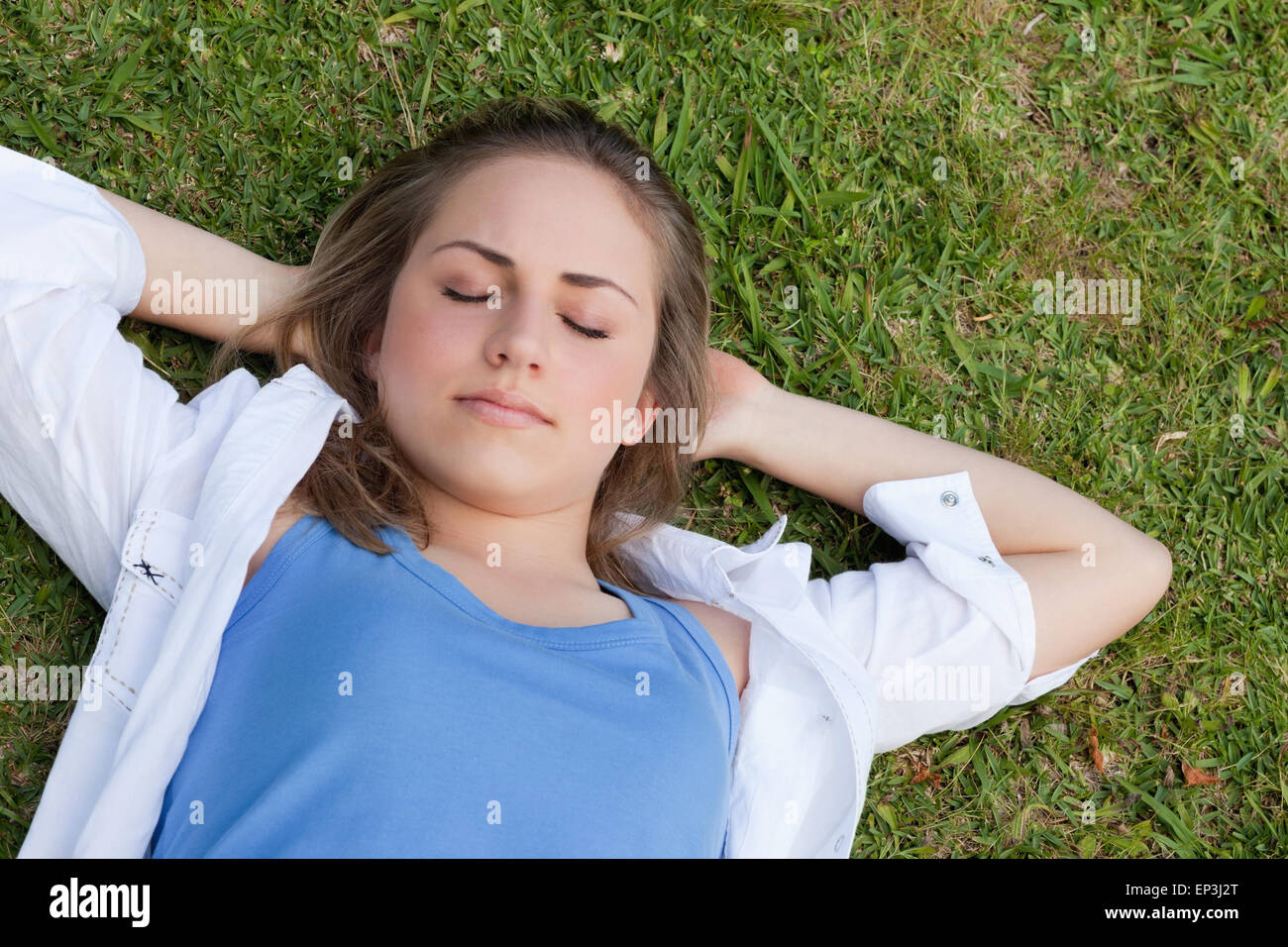 Young relaxed girl napping on the grass while placing her hands behind ...