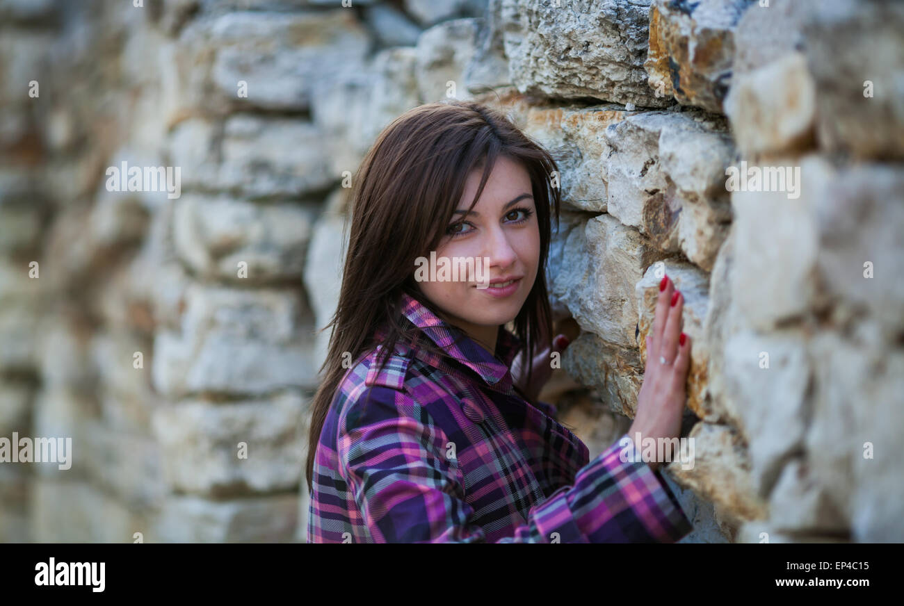 Young woman in sunshine portrait, looks straight to you, near the stone ...