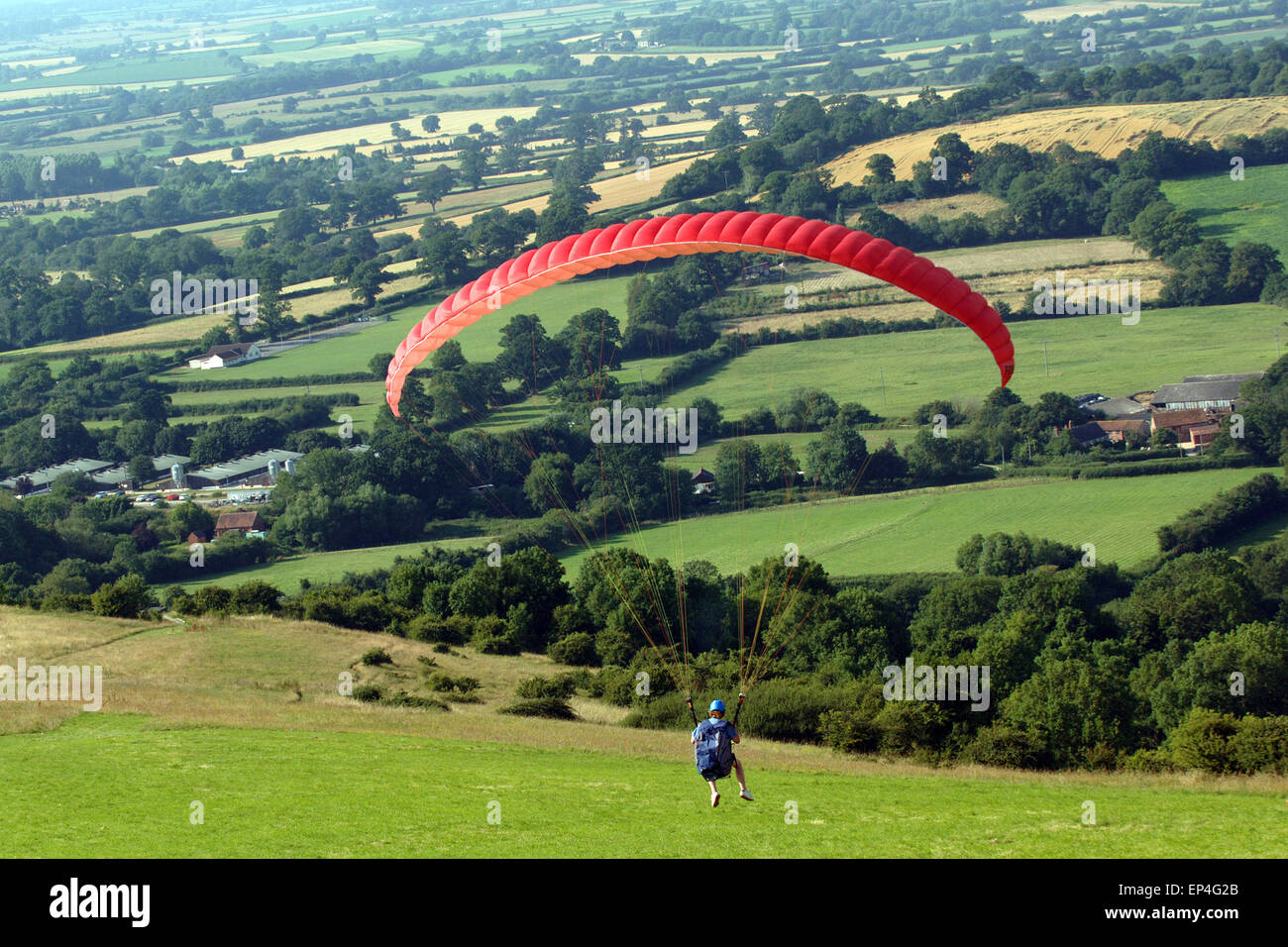 A red paraglider pilot soars over the Dorset countryside.a UK fly flys ...