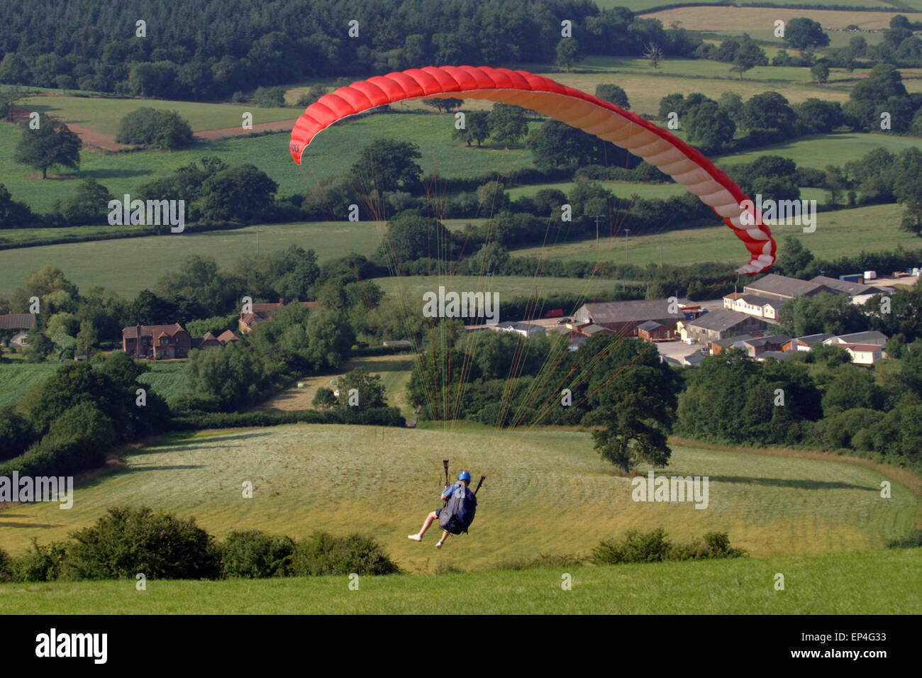 A red paraglider pilot soars over the Dorset countryside.a UK fly flys ...