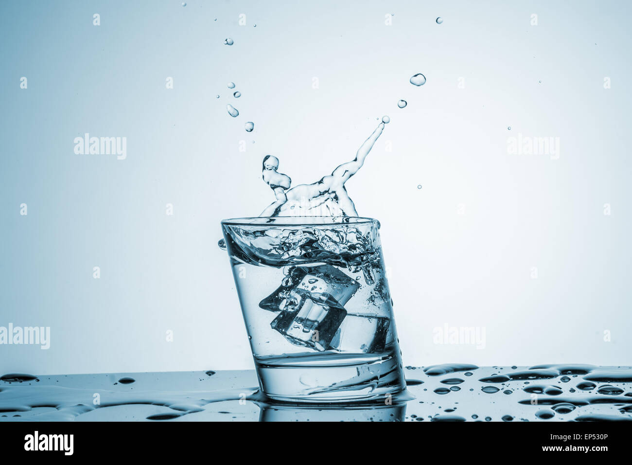 ice cube falling into a glass of water on blue background Stock Photo - Alamy