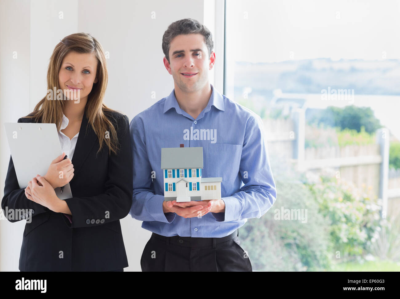 Estate agent holding clipboard and man holding miniature model house ...