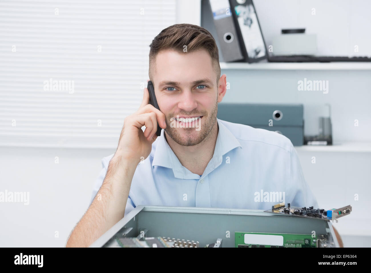 Portrait of smiling computer engineer on call in front of open cpu ...