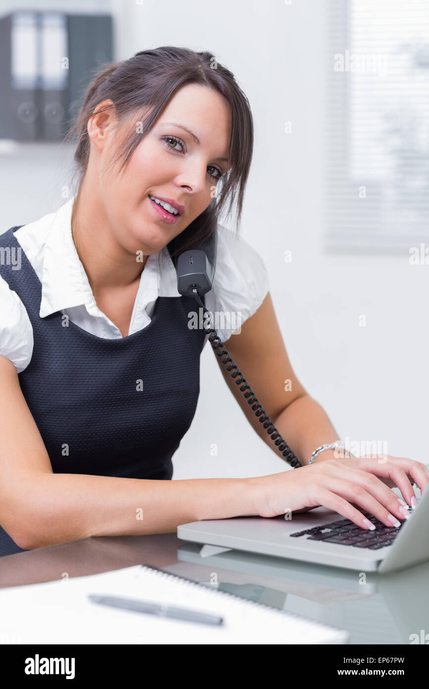 Business woman using landline phone and laptop at desk Stock Photo - Alamy