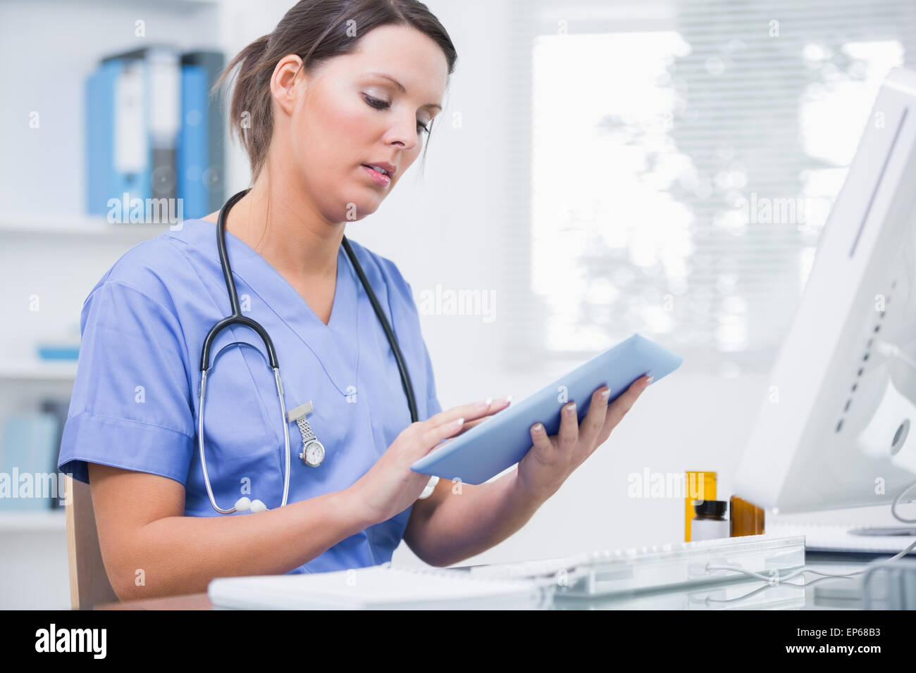 Female surgeon using digital tablet in front of computer at clinic ...