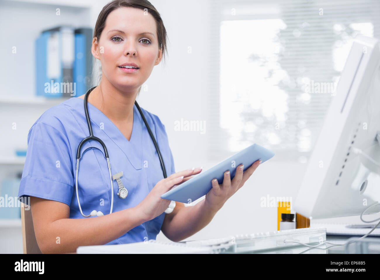 Portrait of surgeon using digital tablet in front of computer at clinic ...