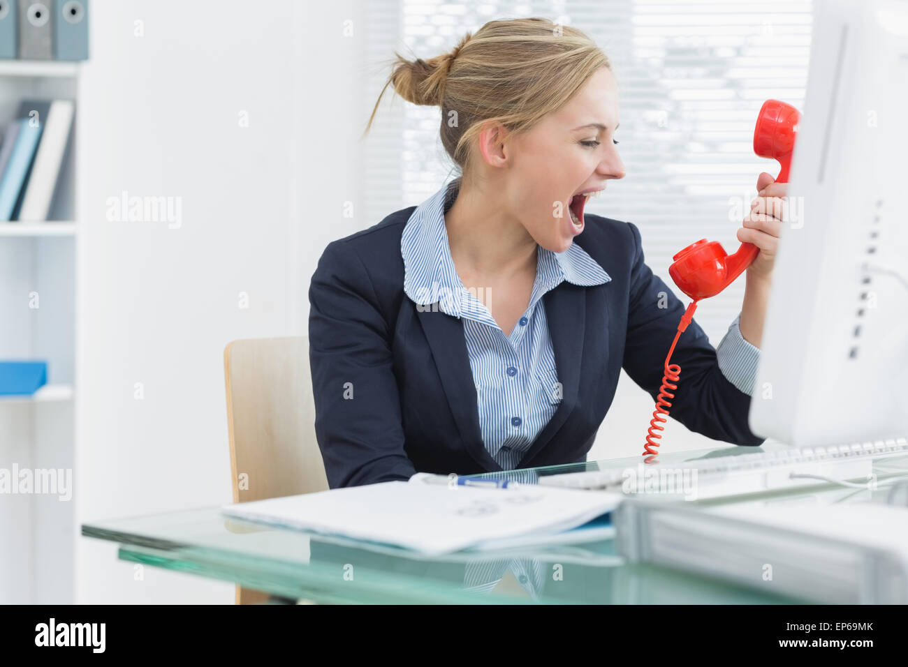 Female executive yelling into red telephone receiver at desk Stock ...