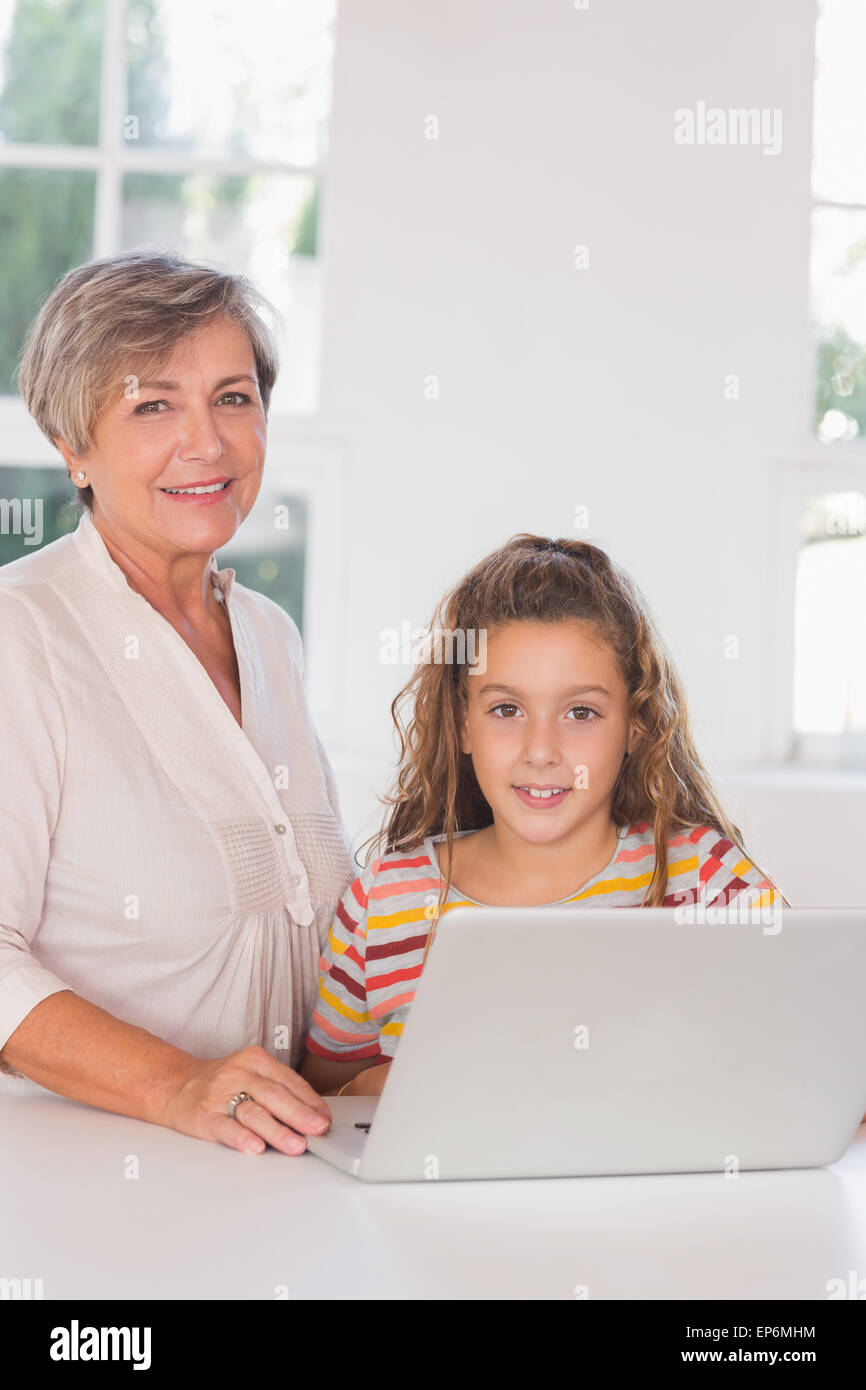 Smiling grandmother and child looking at camera together with laptop ...