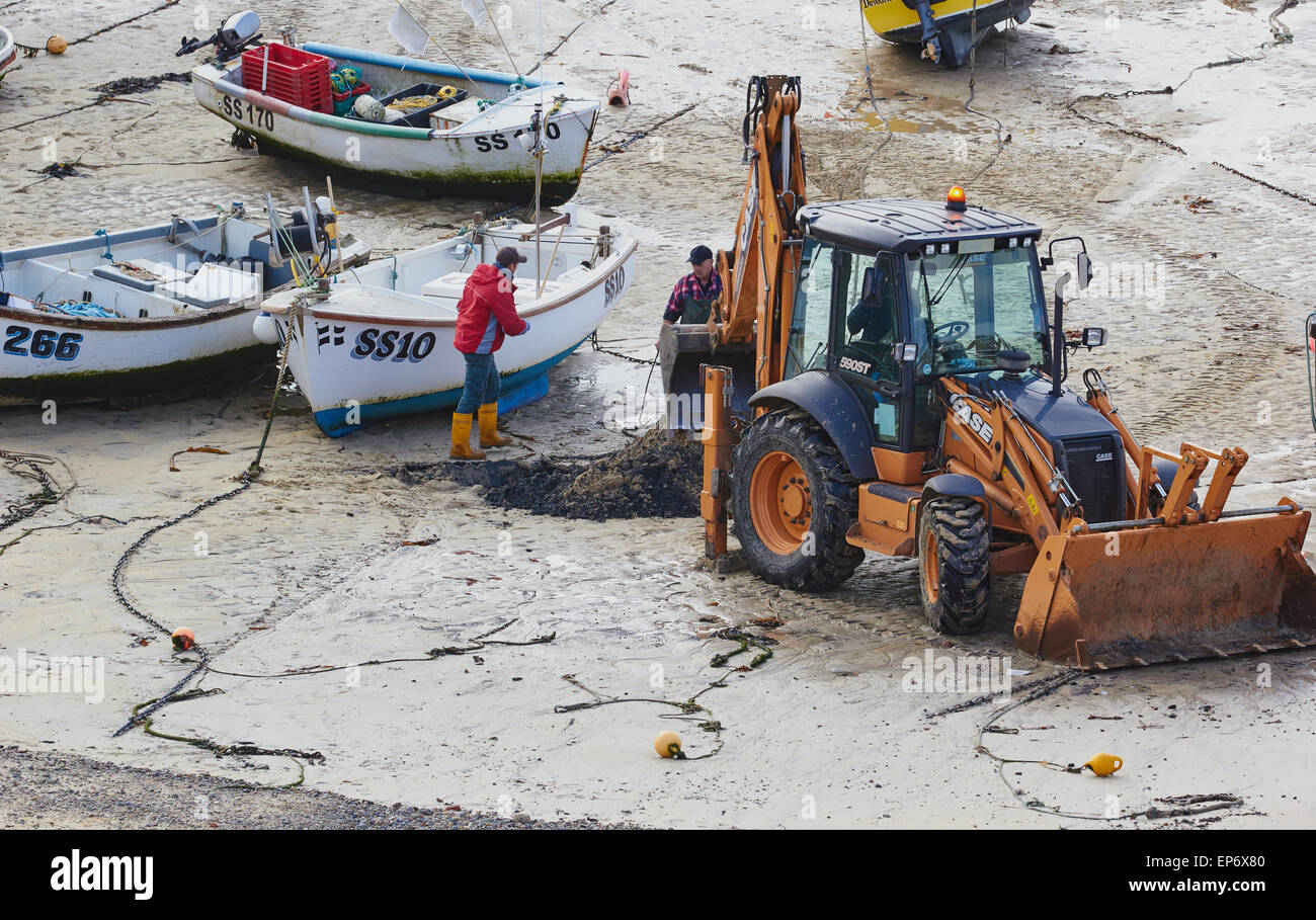 Mechanical digger amongst fishing boats on St Ives harbour beach at low ...