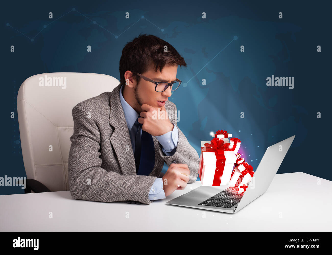 Handsome man sitting at desk and typing on laptop with present boxes ...