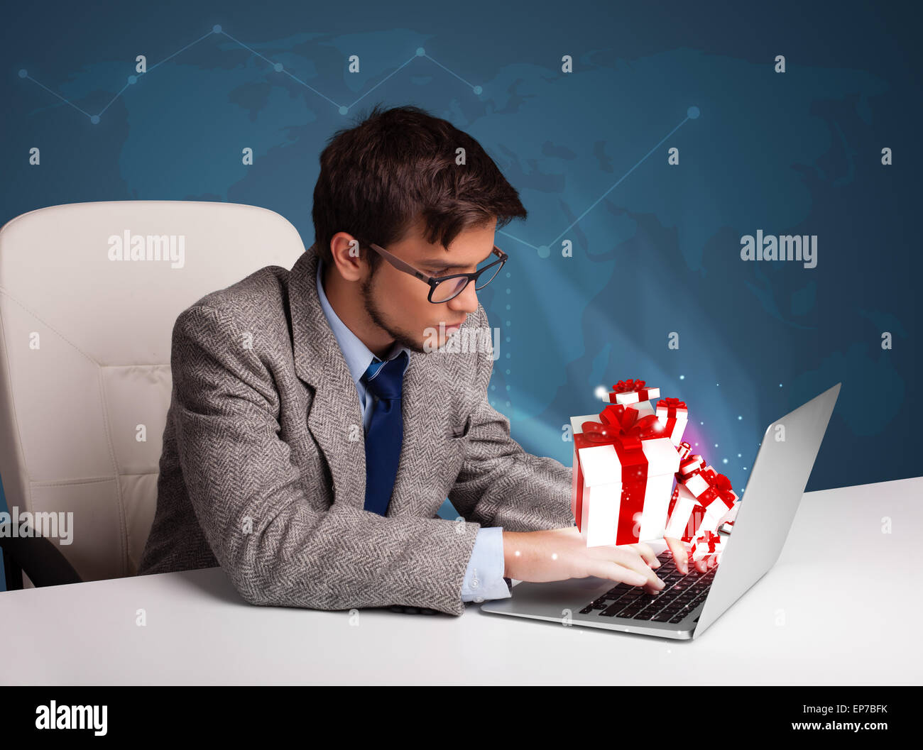 Handsome man sitting at desk and typing on laptop with present boxes ...