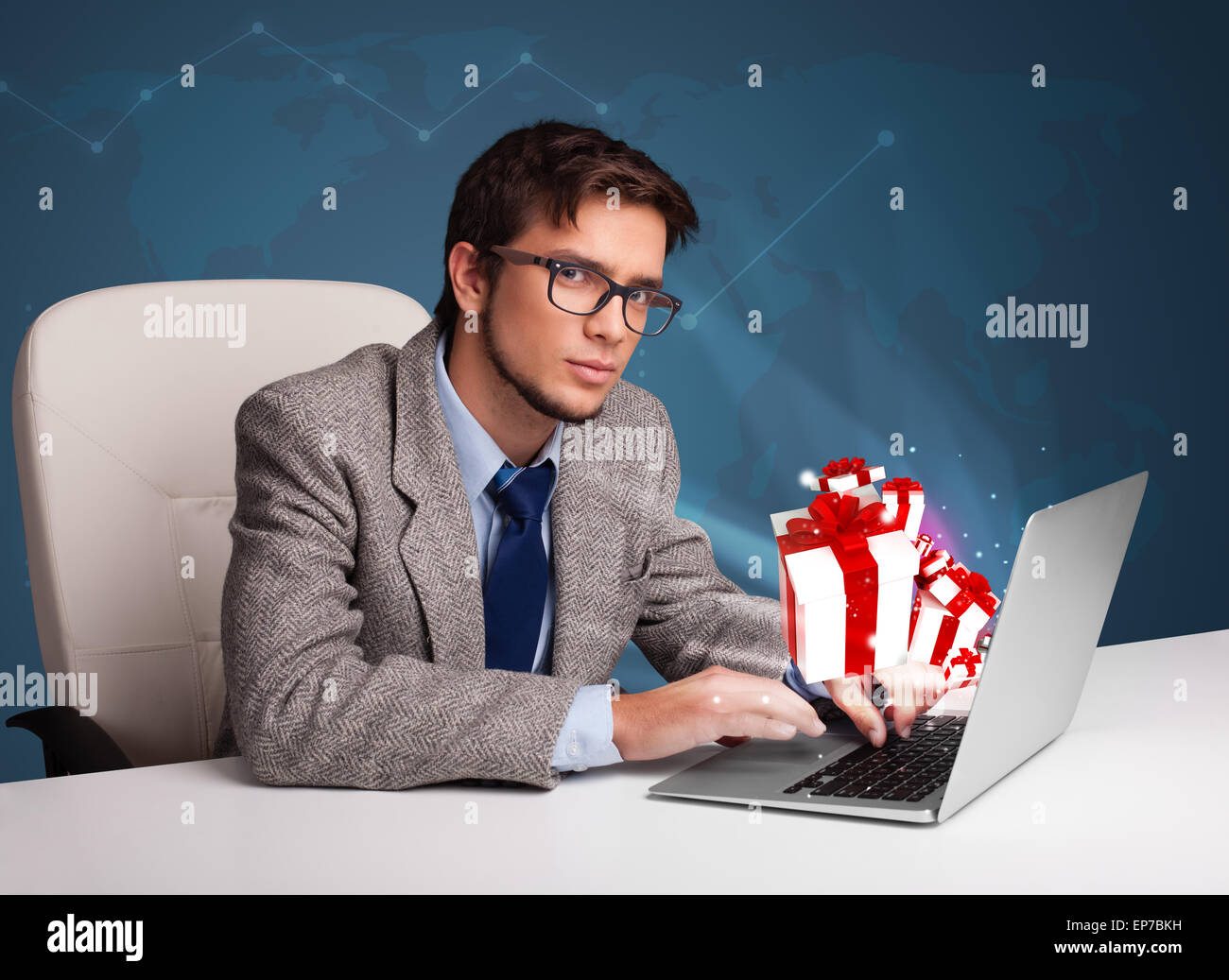 Handsome man sitting at desk and typing on laptop with present boxes ...