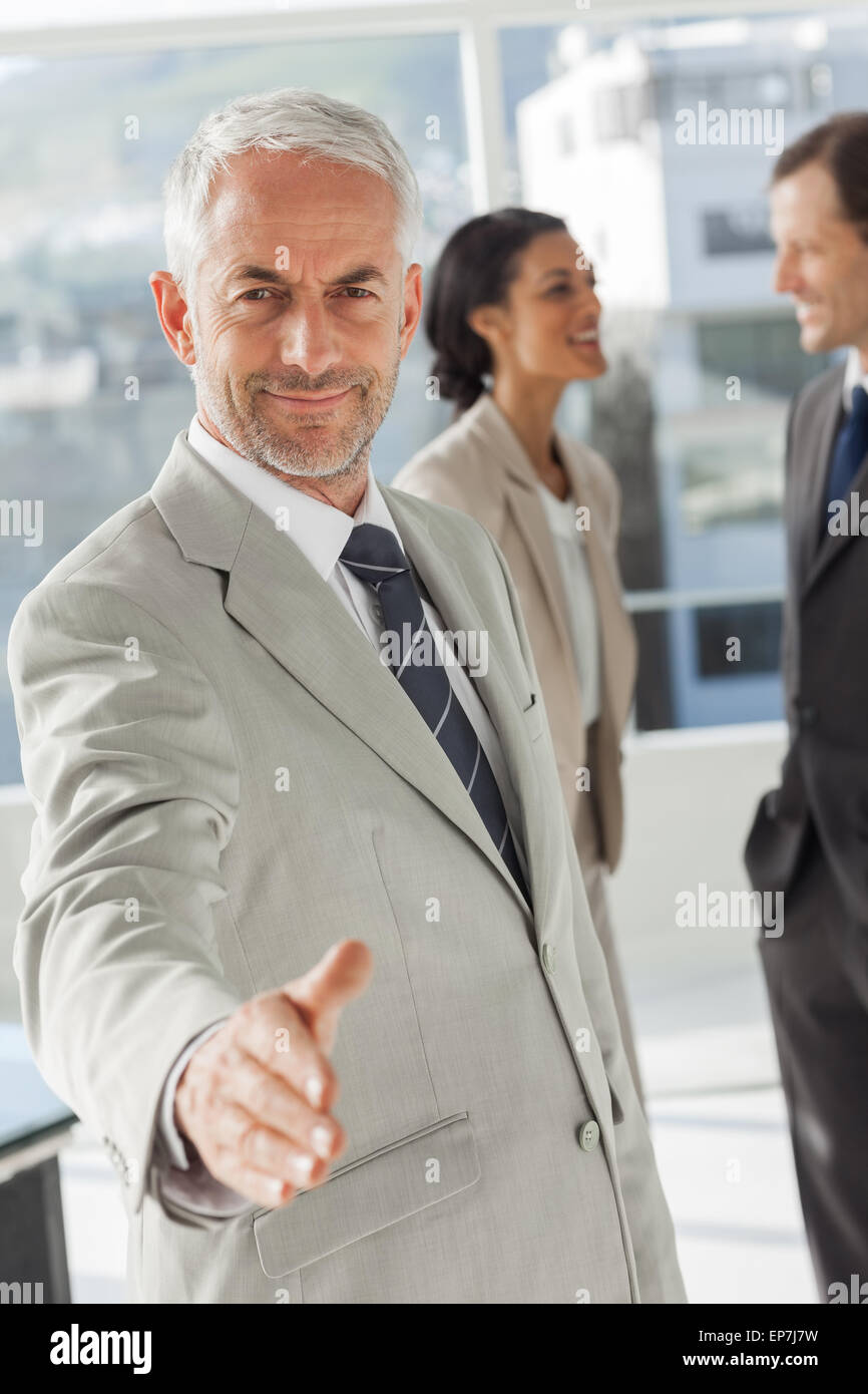 Businessman giving a handshake with colleagues behind Stock Photo - Alamy