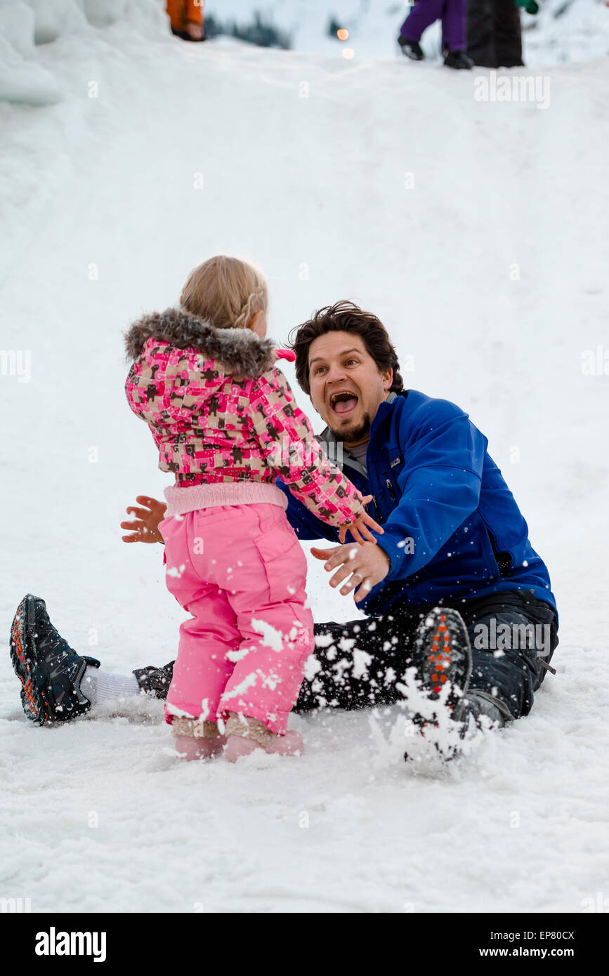 Laughing father slides down snow slide with his young daughter at Squaw ...
