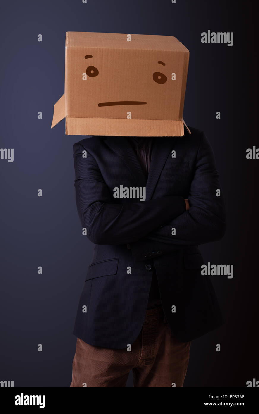 Young man gesturing with a cardboard box on his head with straight face ...