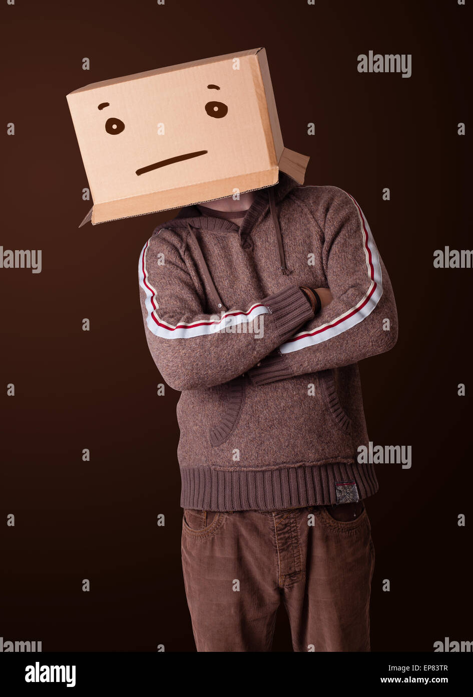 Young man gesturing with a cardboard box on his head with straight face ...