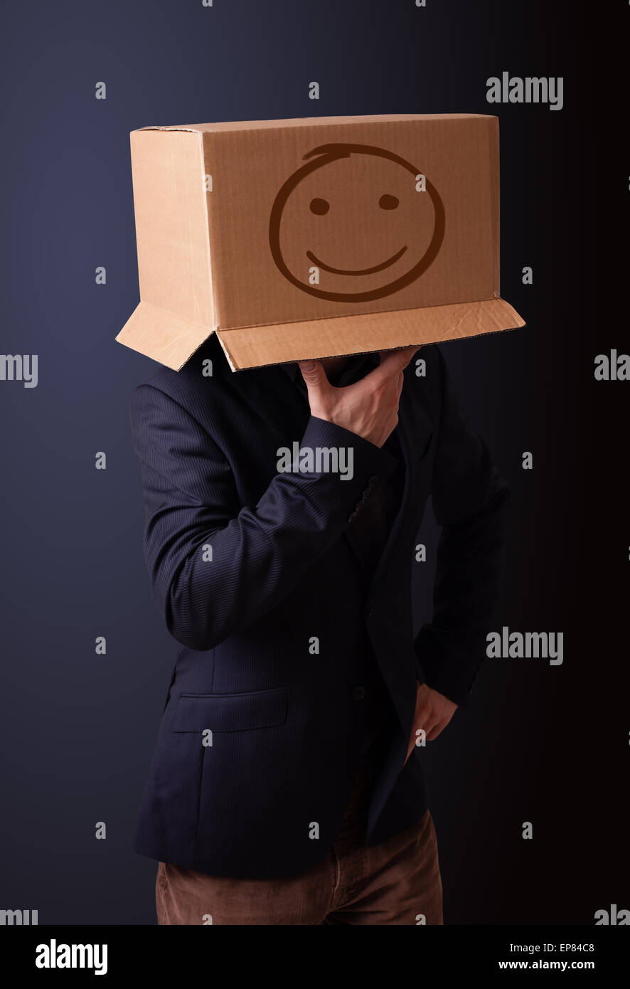 Young man gesturing with a cardboard box on his head with smiley face ...