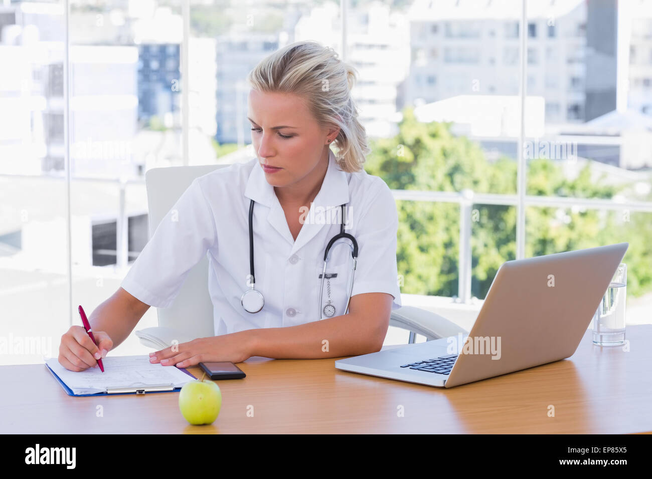 Blonde nurse writing on a notepad on her desk Stock Photo - Alamy