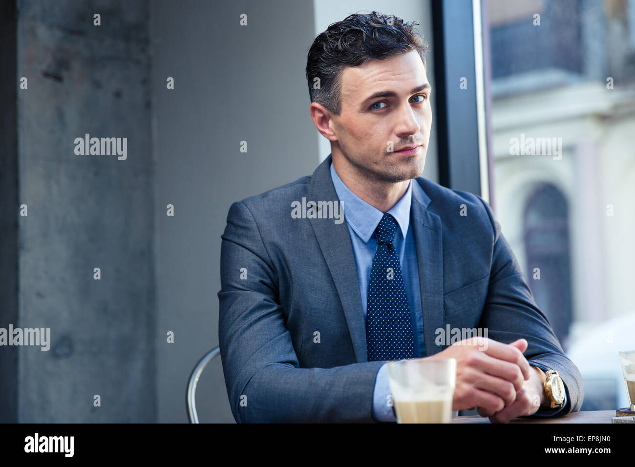Handsome businessman sitting at the table in cafe and looking at camera ...