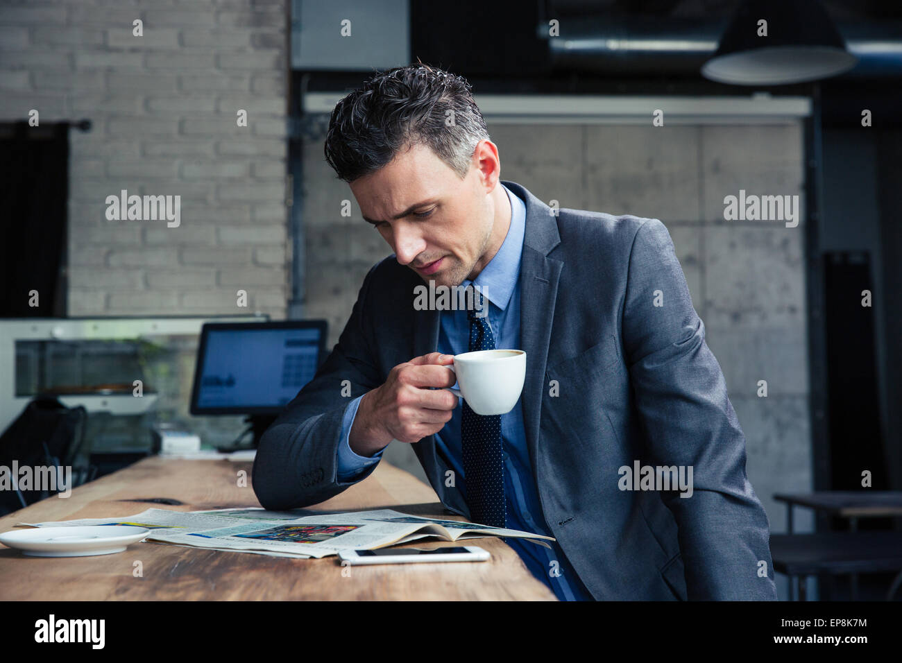 Confident businessman reading magazine and drinking coffee in cafe ...