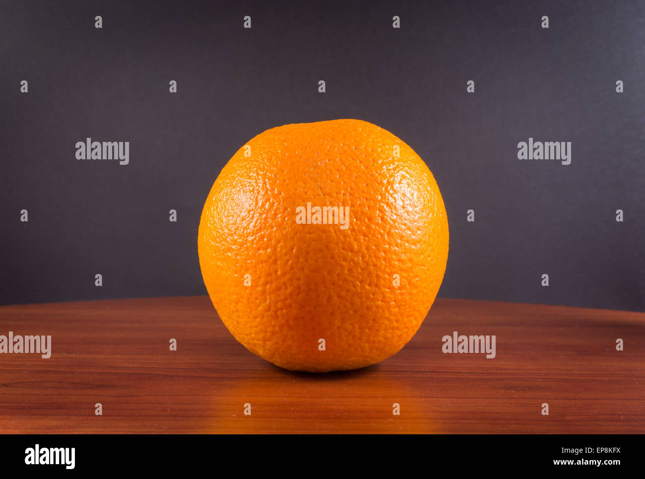Single ripe orange on wooden rustic surface with grey black background ...