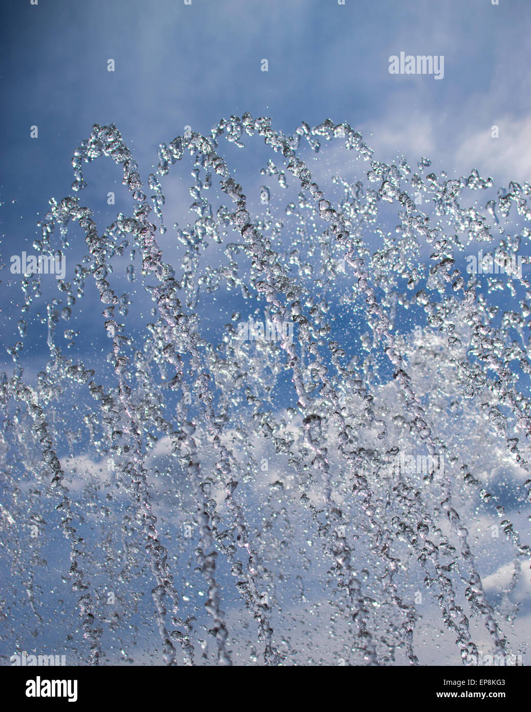 Water spraying from a fountain against a blue sky with white clouds ...