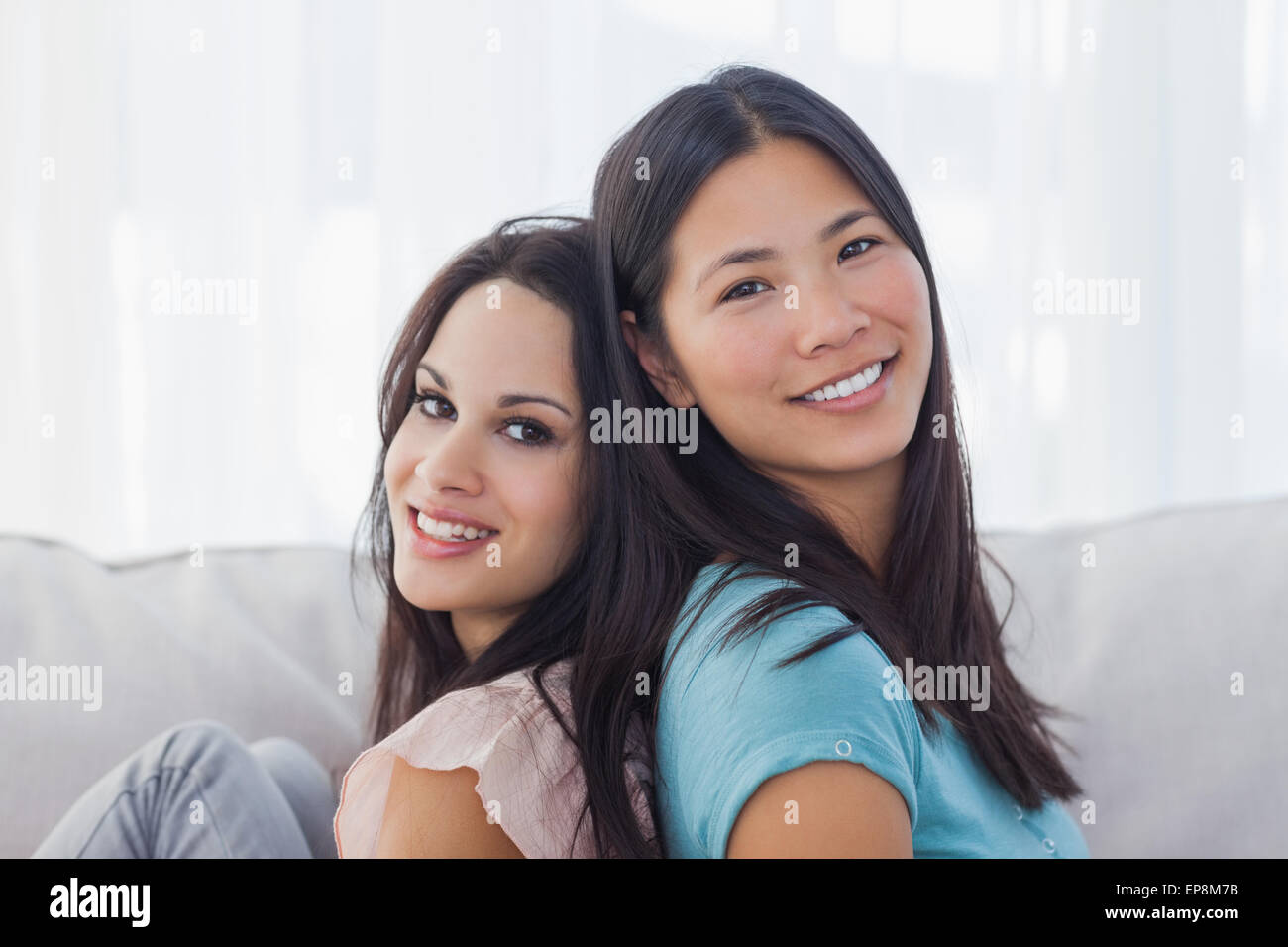 Friends sitting back to back smiling at camera Stock Photo - Alamy