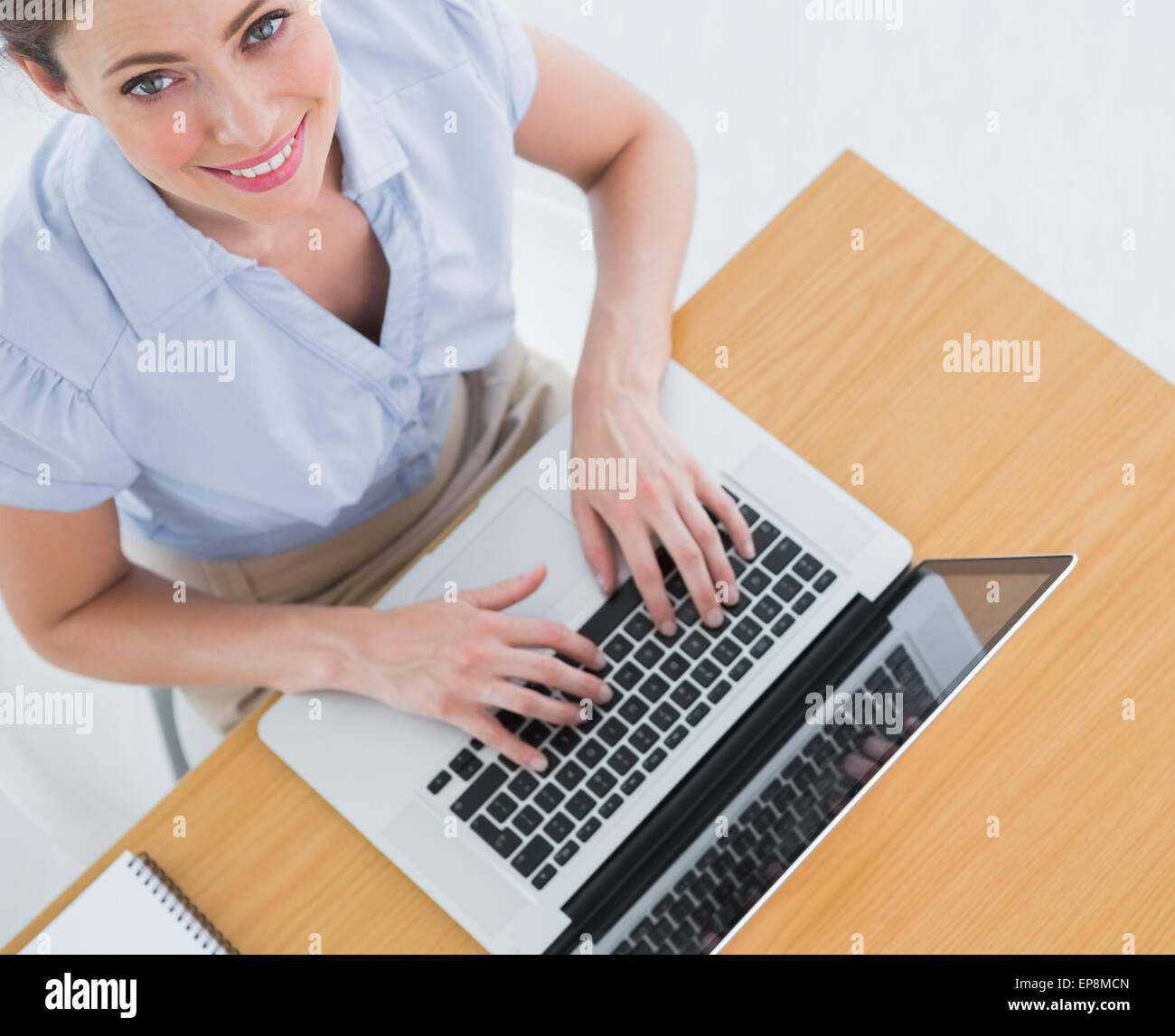 Pretty businesswoman typing on her laptop and smiling up at camera ...