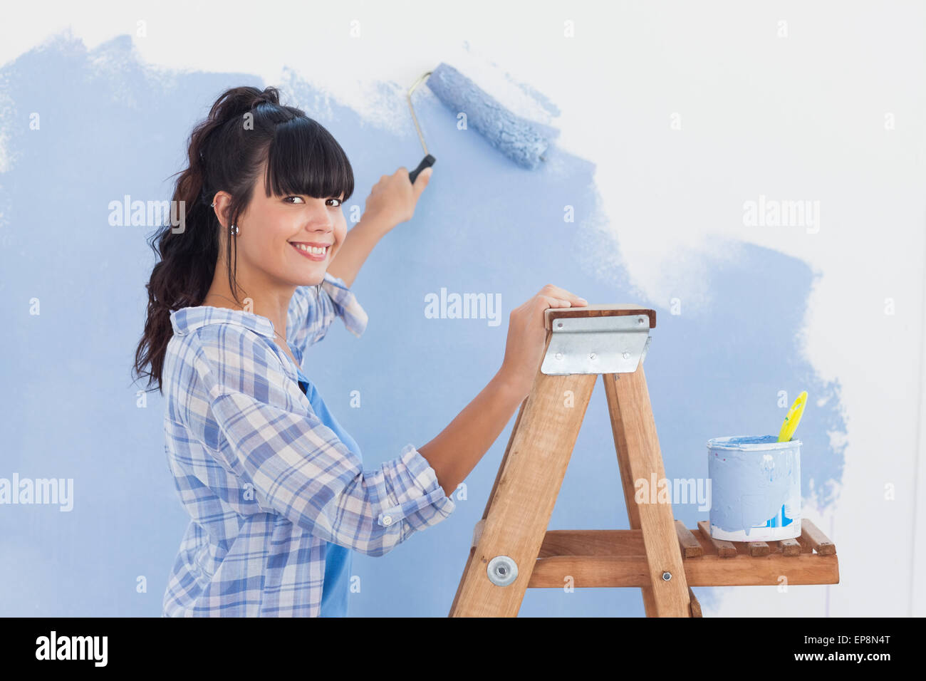 Woman using paint roller to paint wall and smiling at camera Stock ...