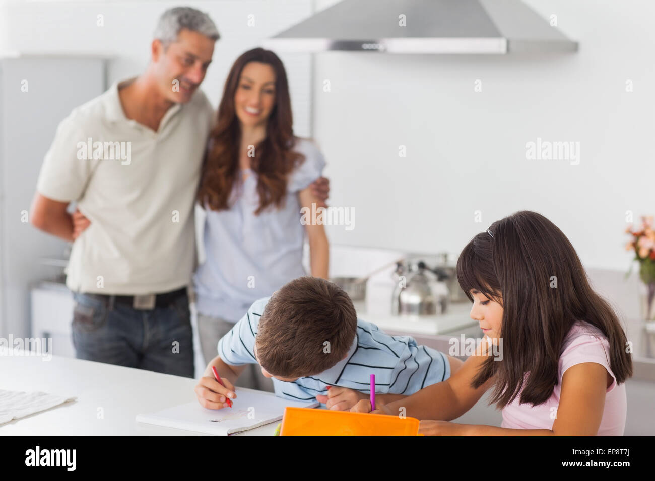 Cute siblings drawing together in kitchen with their parents smiling ...