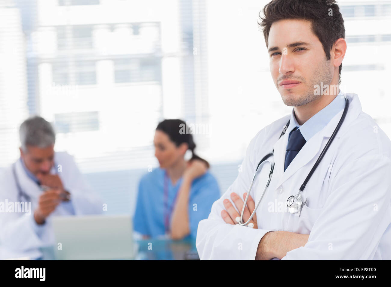 Serious doctor looking at camera with colleagues behind Stock Photo - Alamy