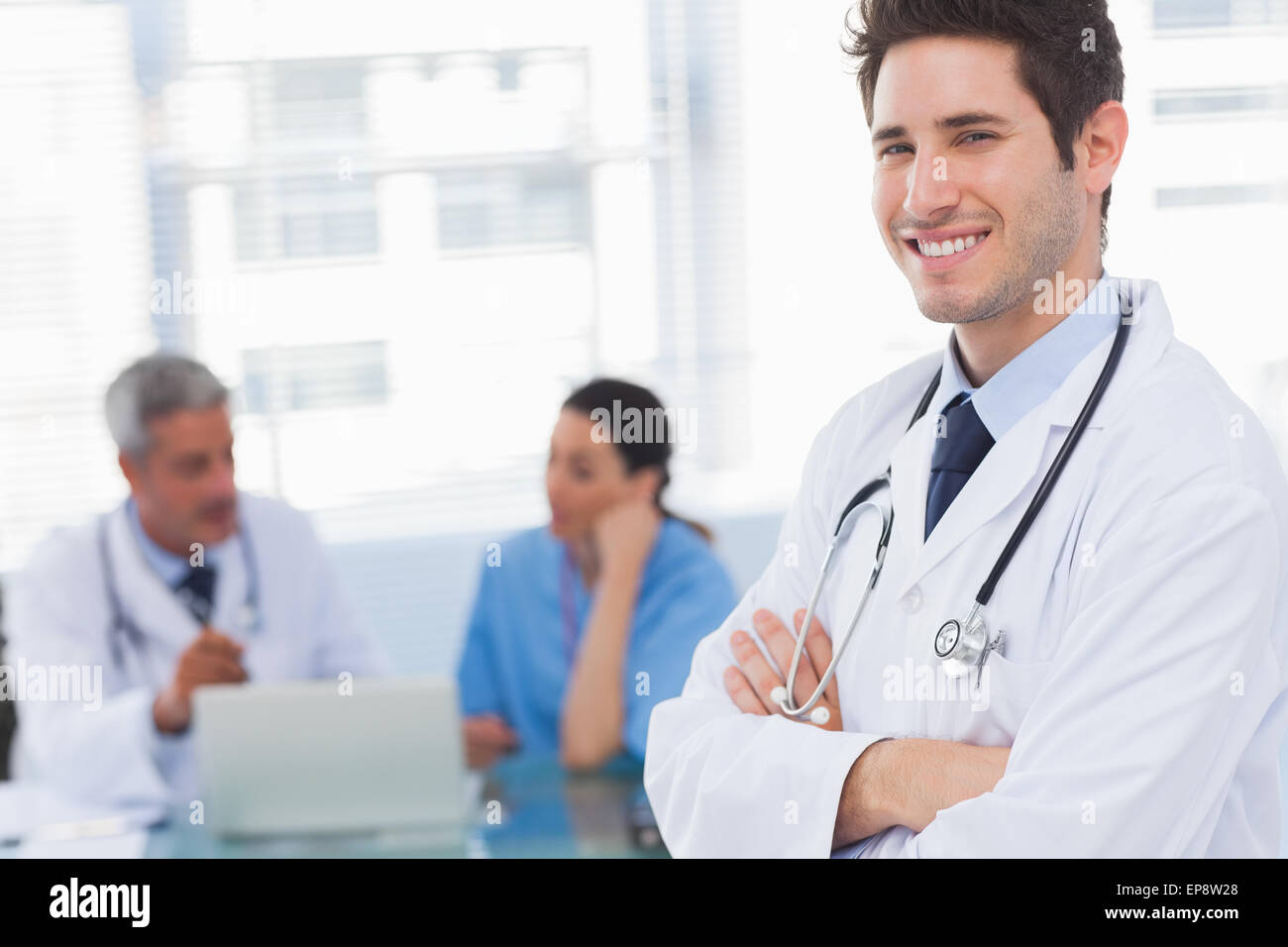 Happy doctor looking at camera with colleagues behind Stock Photo - Alamy