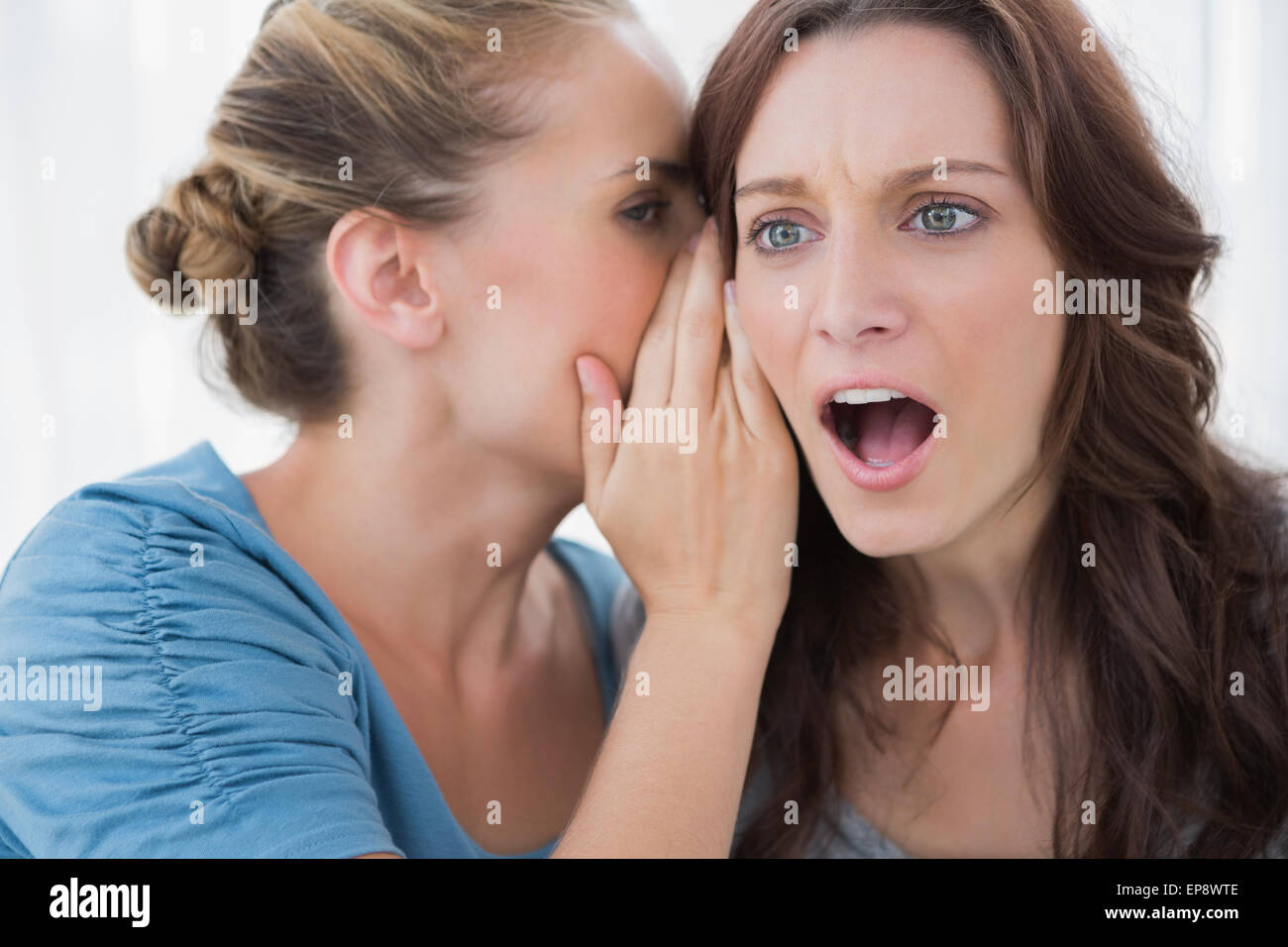 Stunned woman being told a secret by her friend Stock Photo - Alamy