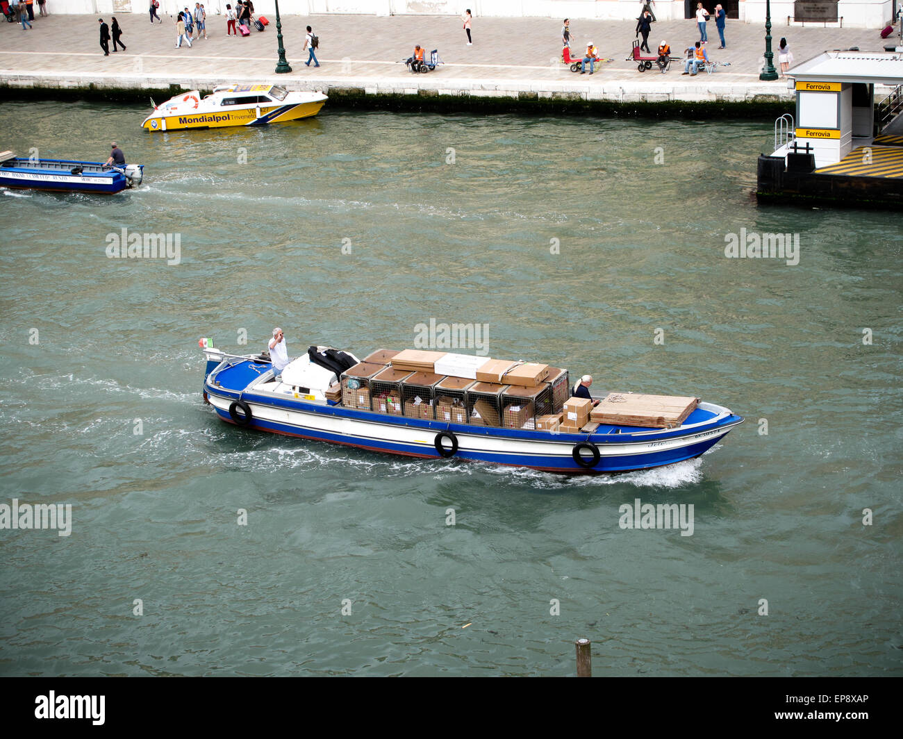 A blue commercial boat loaded with goods on the Grand Canal in Venice ...