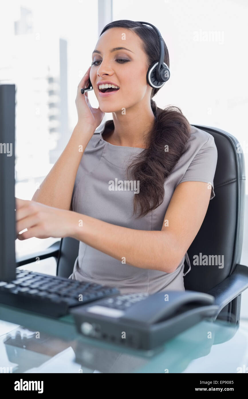 Attractive secretary wearing headset and pointing at computer screen ...