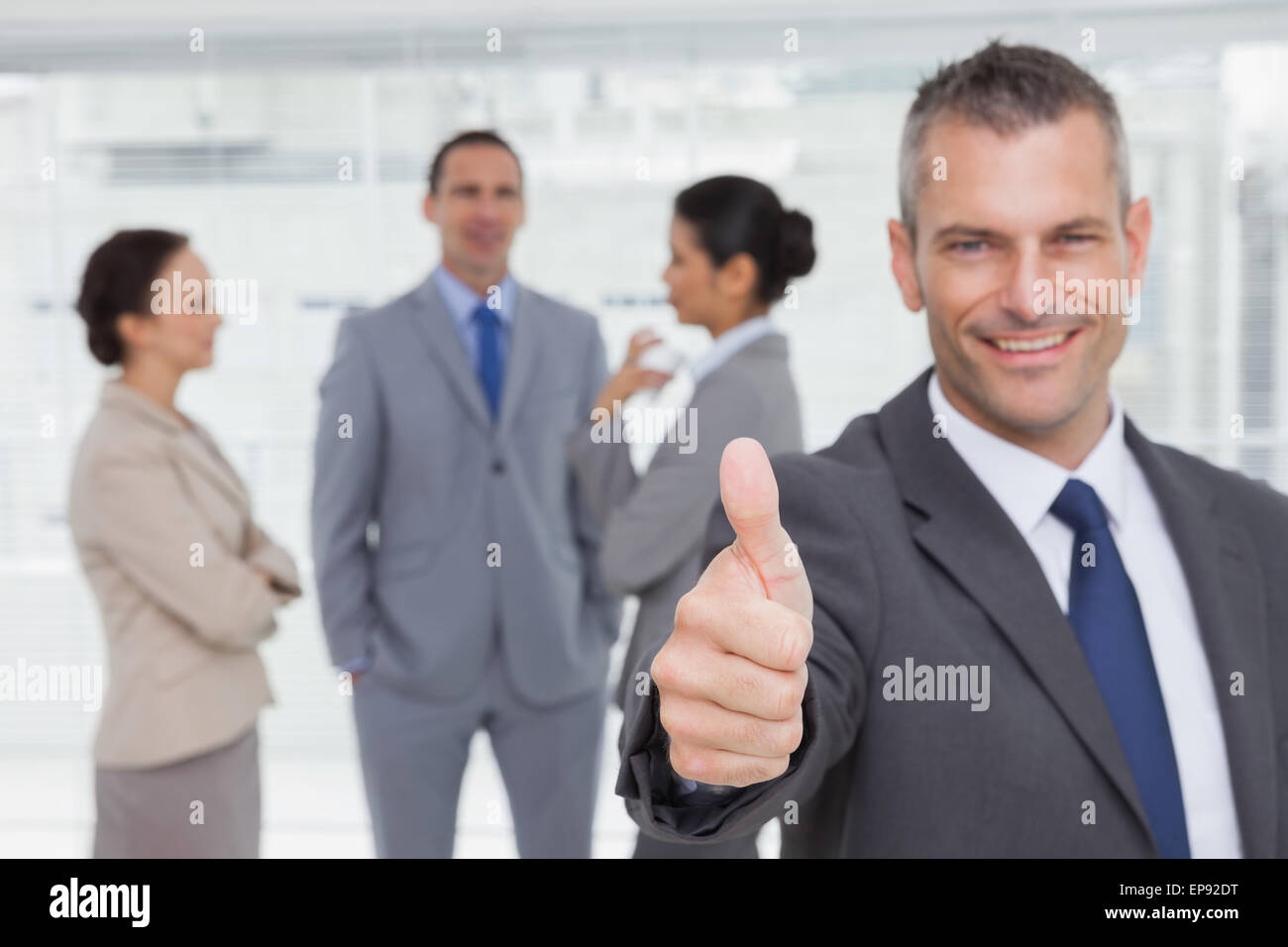 Cheerful manager showing thumb up with employees in background Stock ...