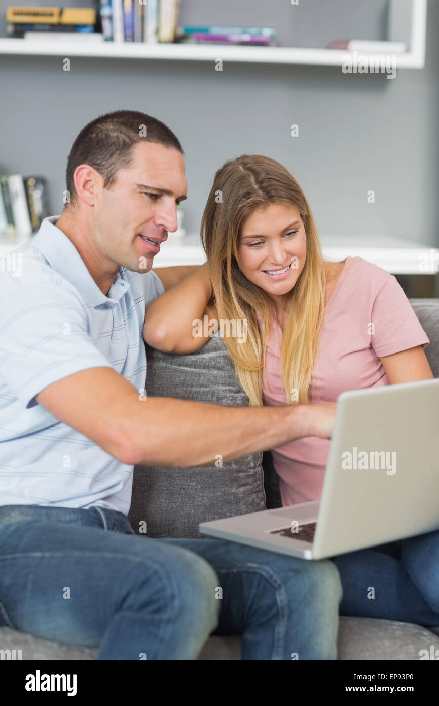 Cheerful couple sitting using laptop on the sofa together Stock Photo ...