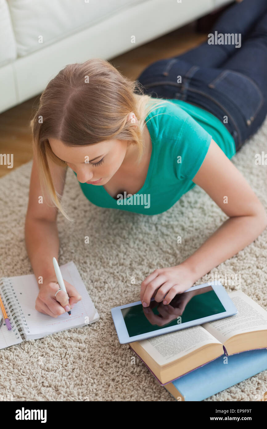 Focused young woman lying on floor using tablet to do her assignment ...