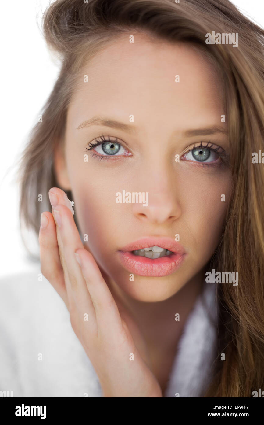 Pensive brunette in bathrobe rubbing her cheek with cream Stock Photo ...