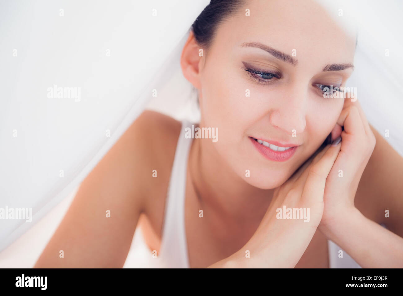 Happy brunette lying under the sheets looking down Stock Photo - Alamy
