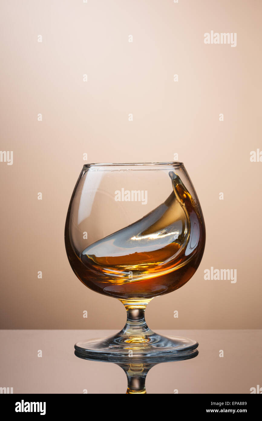 Splash of cognac in glass on brown background Stock Photo - Alamy