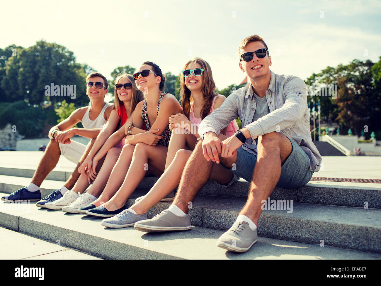 group of smiling friends sitting on city street Stock Photo - Alamy