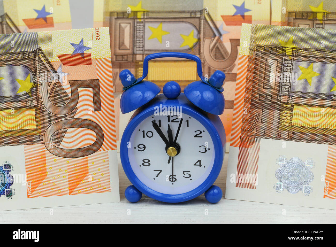 Miniature clock with banknotes in the background Stock Photo - Alamy