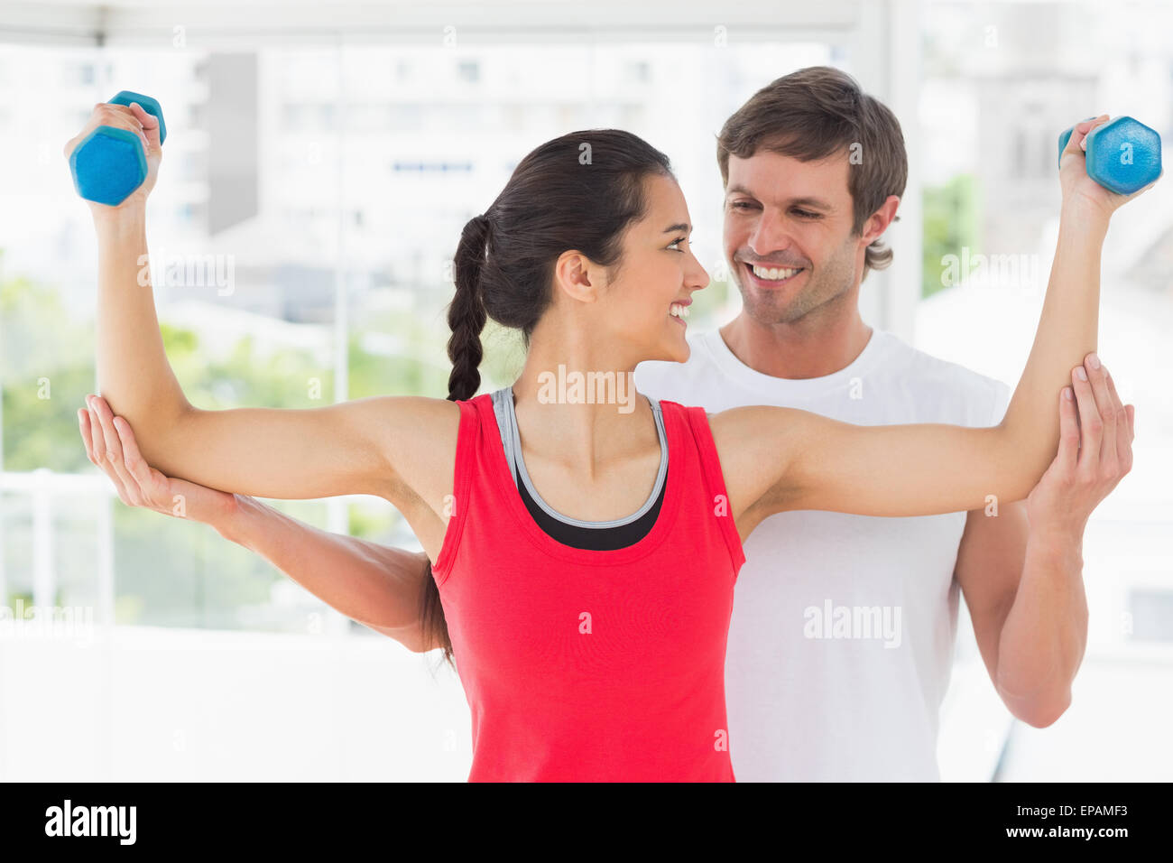 Smiling instructor with woman lifting dumbbell weights Stock Photo - Alamy