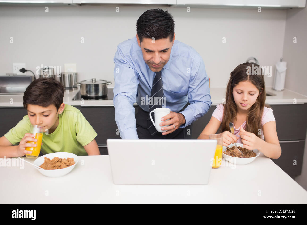 Father using laptop and kids having breakfast in kitchen Stock Photo ...